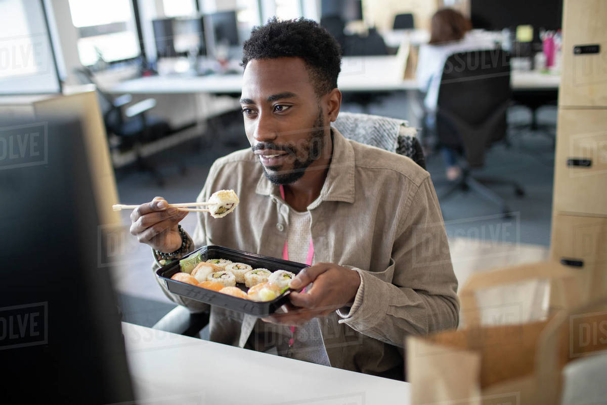 Businessman eating sushi takeout lunch at computer in office - Royalty ...