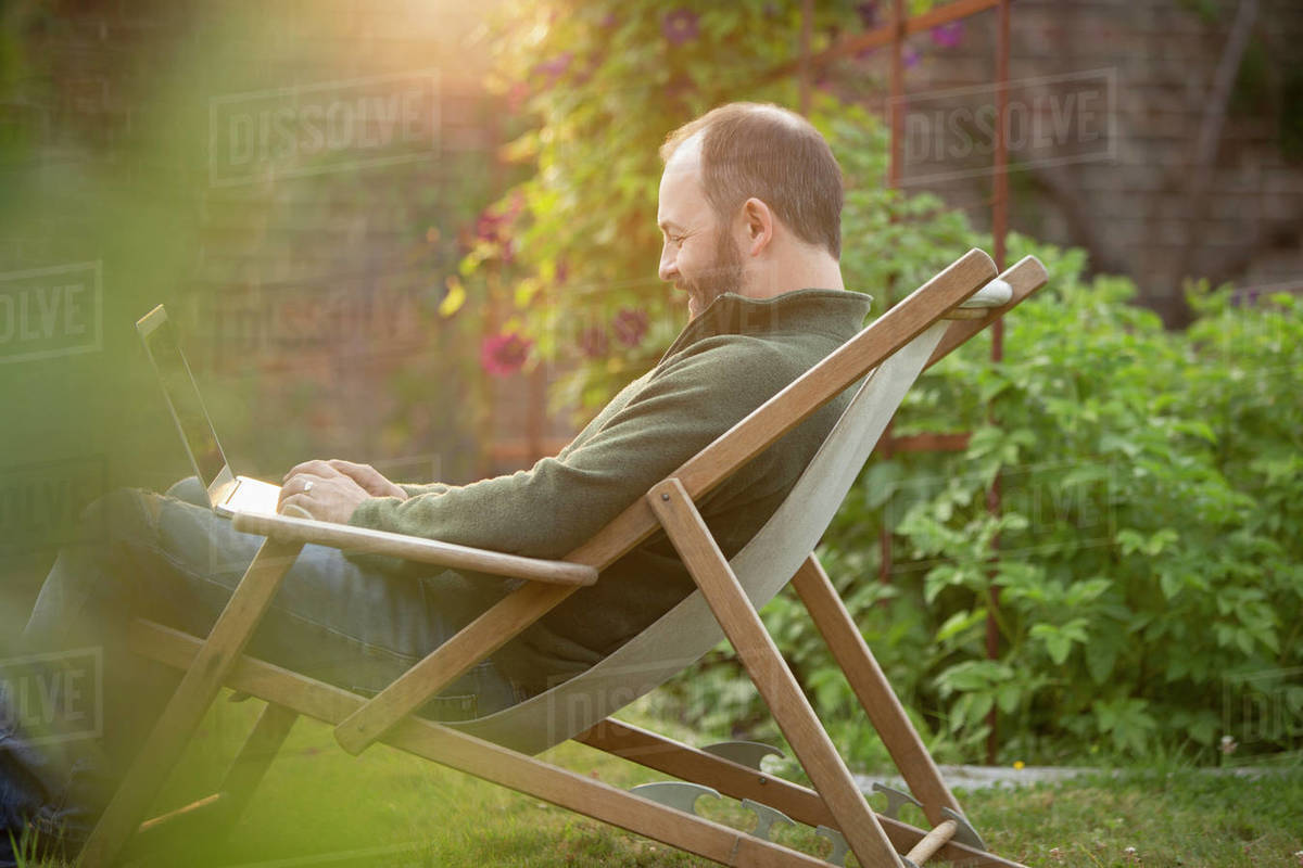 Man working at laptop in lawn chair in summer garden - Royalty-free ...