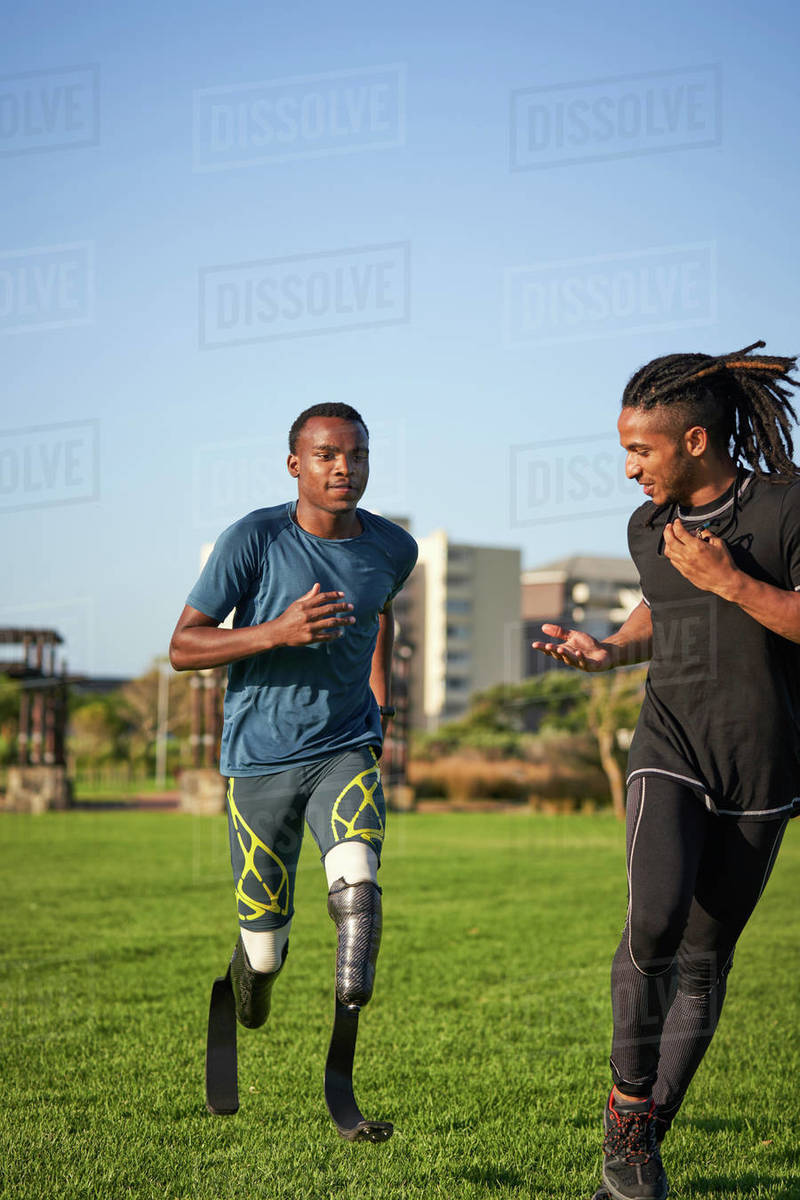Trainer timing male amputee athlete running in sunny grass - Royalty ...