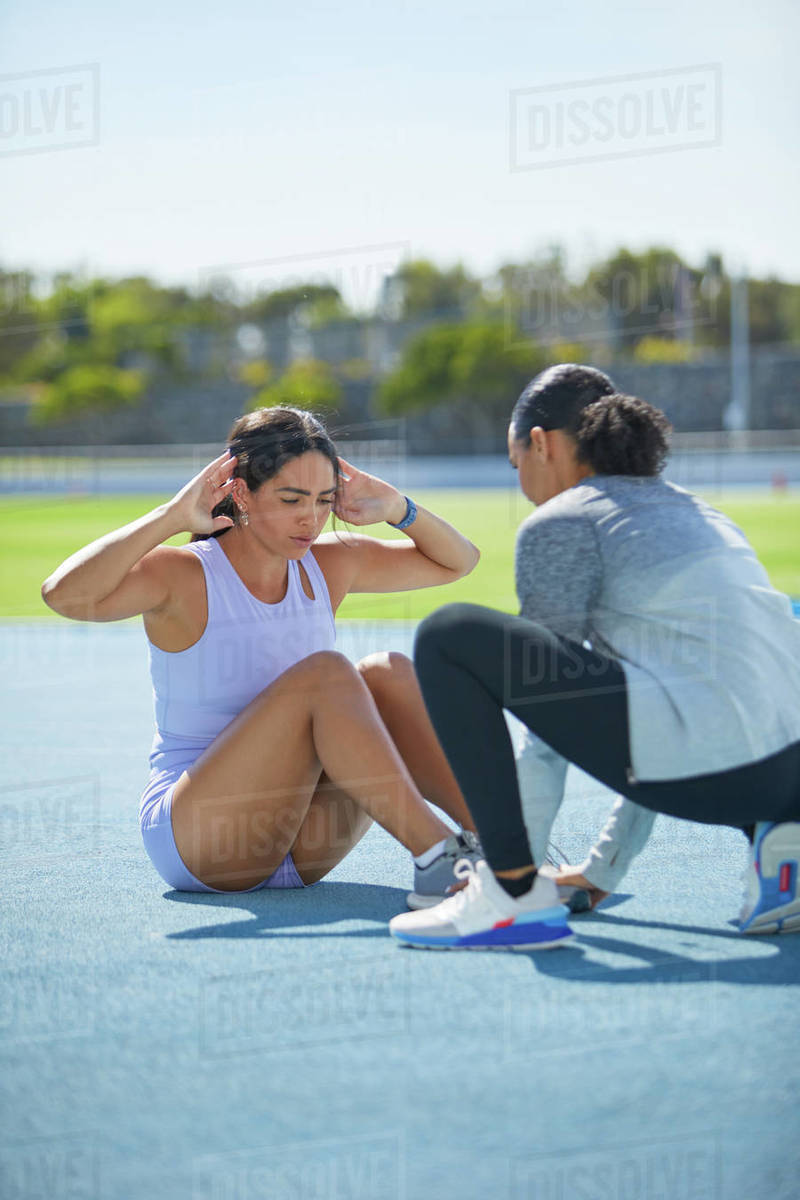 Female track and field athletes doing sit ups on sunny track - Stock ...