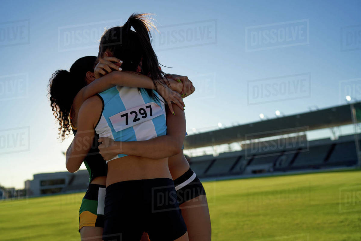 Happy female track and field athletes hugging in stadium infield ...