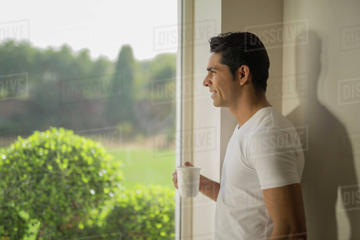 Smiling man at window holding coffee cup - Stock Photo - Dissolve