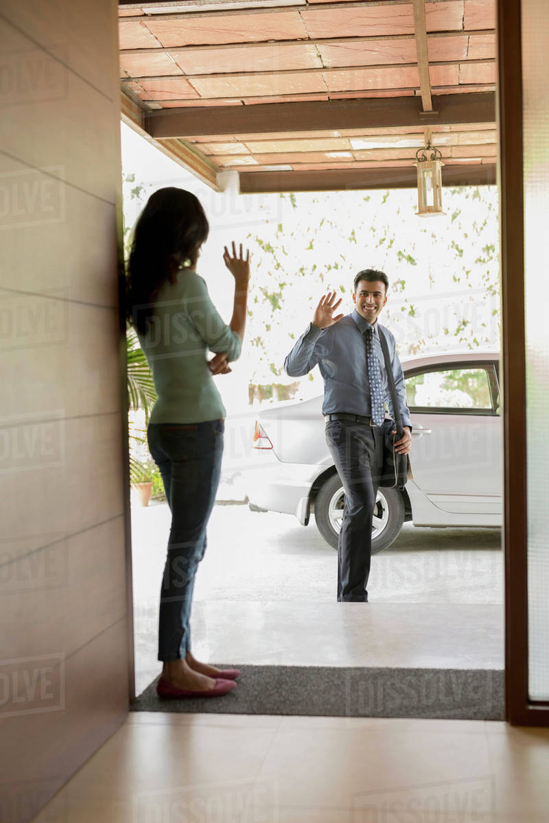 Man and woman waving goodbye at front door - Stock Photo - Dissolve