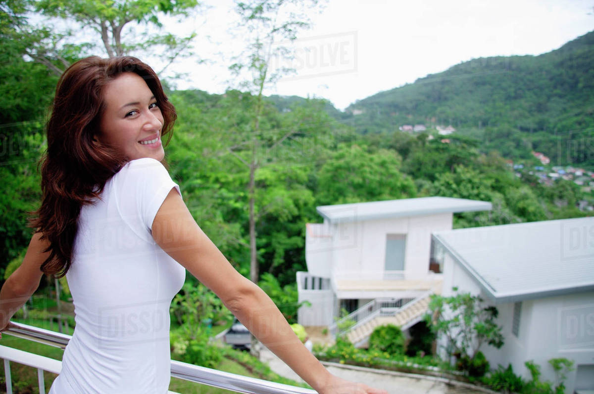 Young woman leaning on railing, looking over shoulder at camera ...