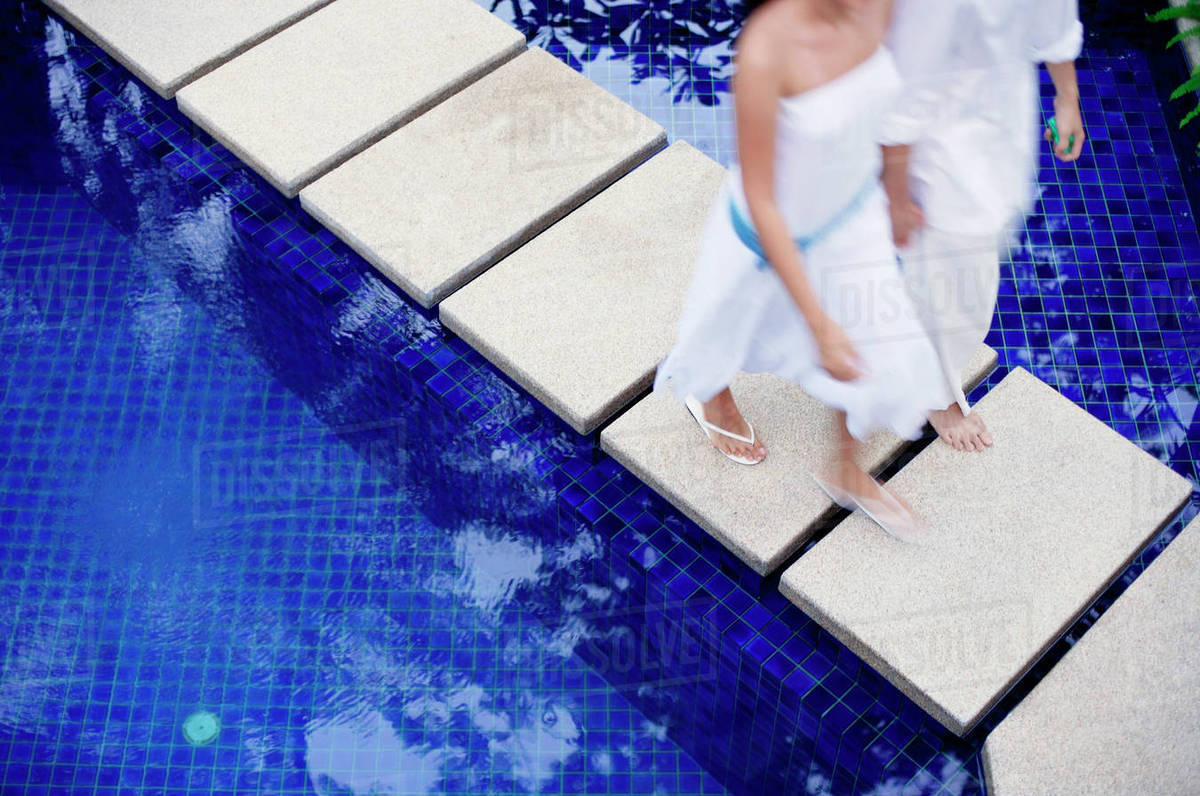 Couple walking on walkway across pool - Royalty-free Stock Photo | Dissolve