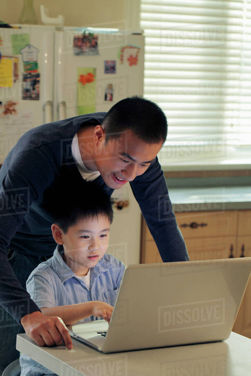 Father and son working on laptop computer together - Stock Photo - Dissolve