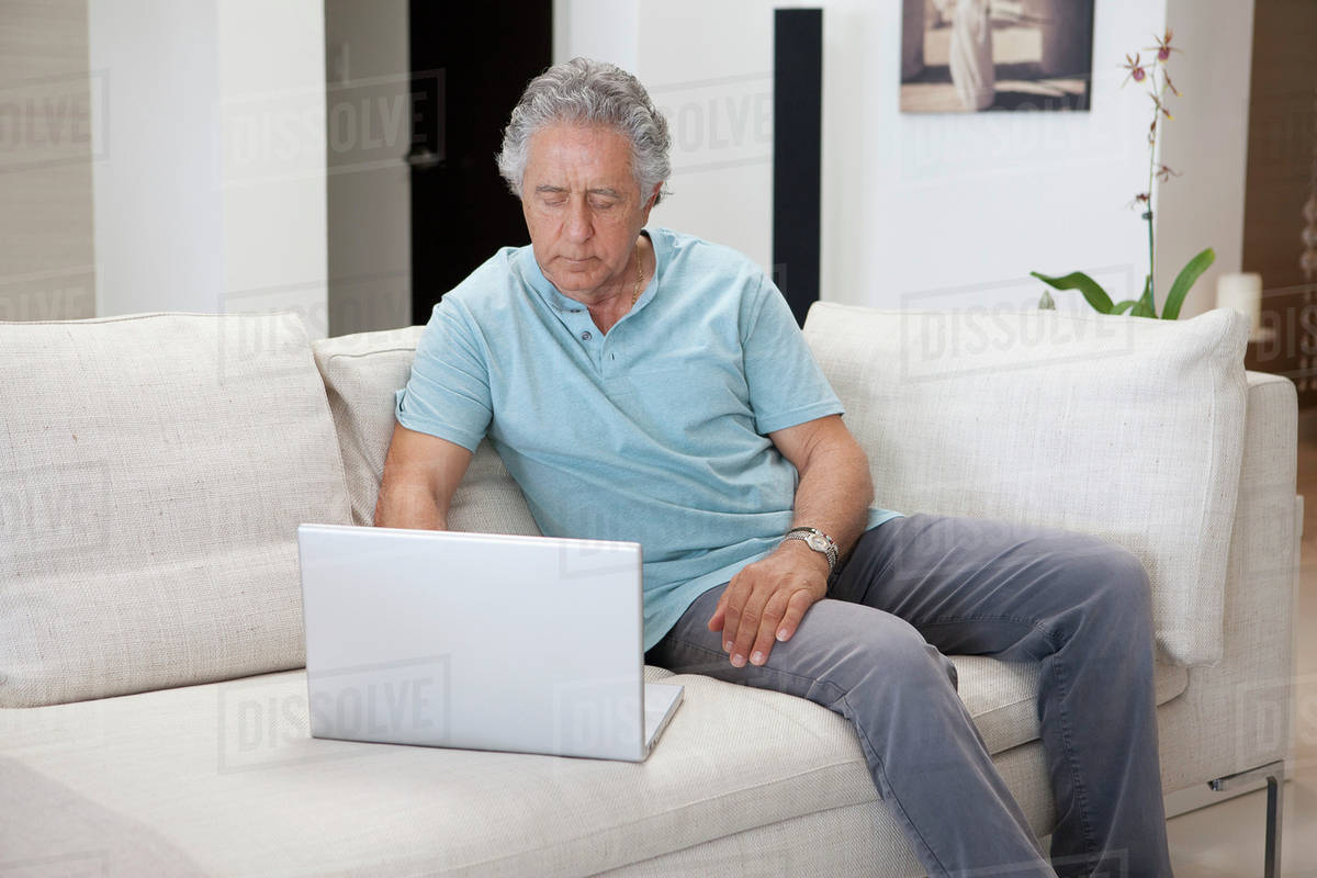 A senior man sitting on a couch using a laptop - Stock Photo - Dissolve