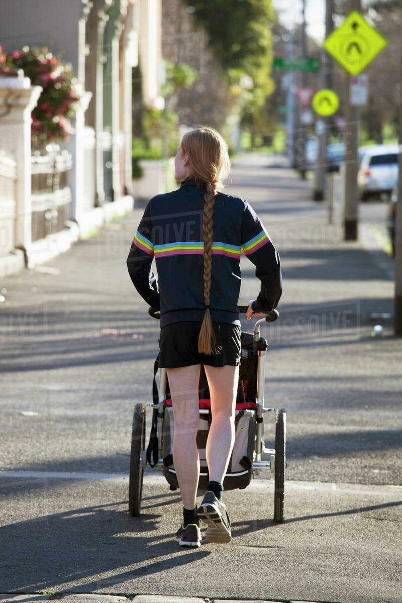 Rear view of a woman walking on a sidewalk with a pram - Royalty-free ...