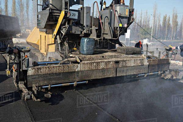 Manual workers controlling large road surfacing machine being trailed ...