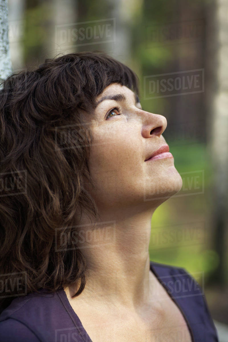 A beautiful woman looking up serenely while leaning against a tree ...