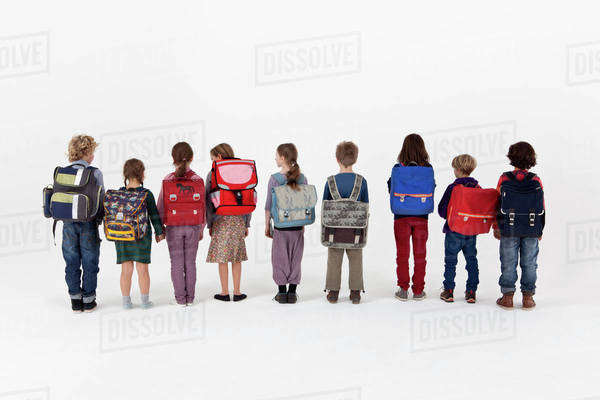A group of school children wearing backpacks and standing in a row ...