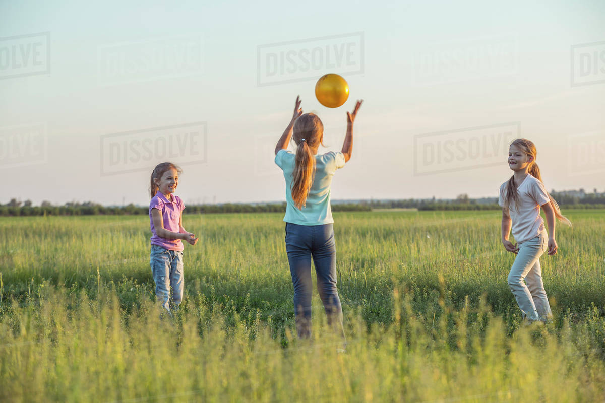 Three young girls playing catch in a sunny field in summer - Stock ...