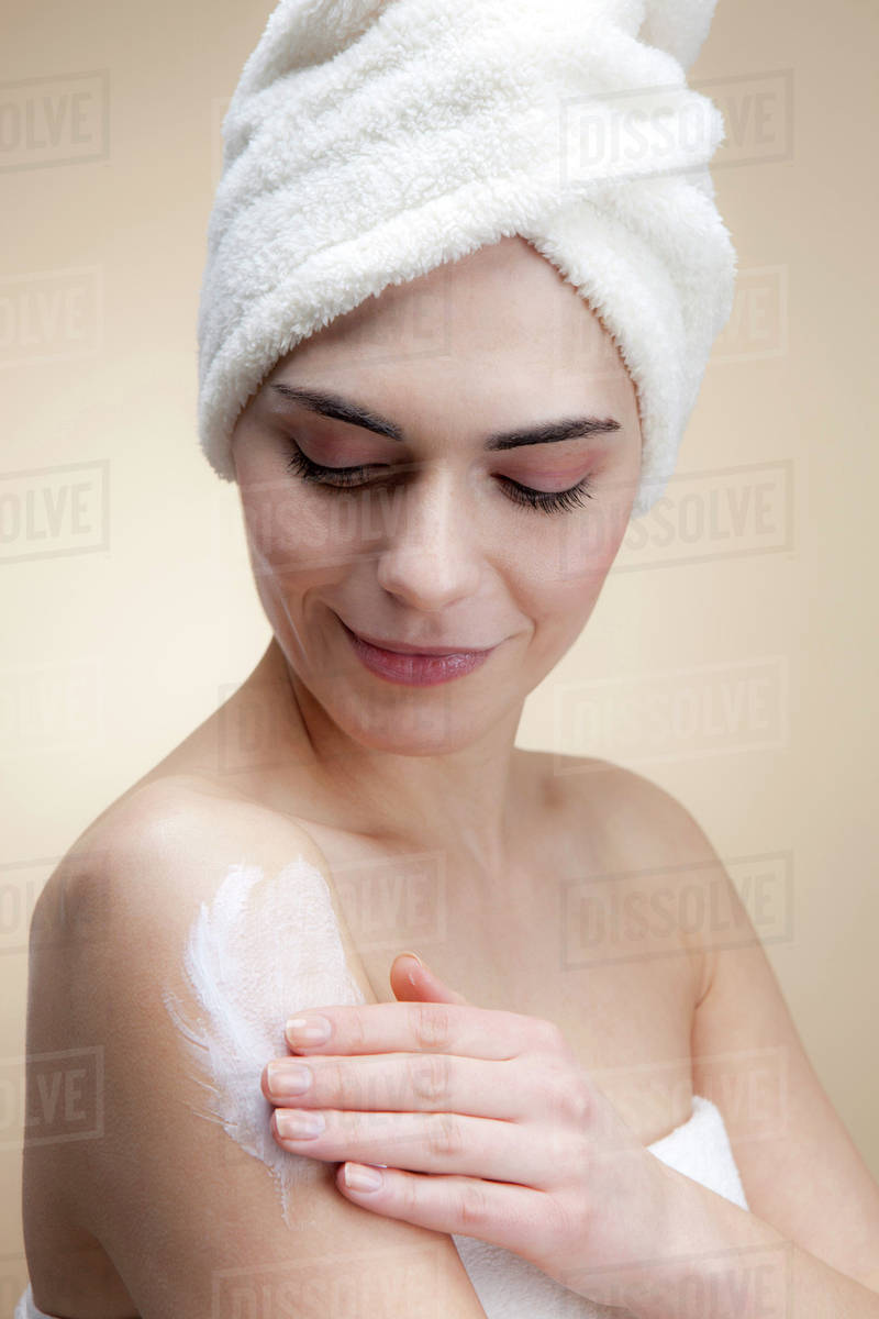A smiling young woman applying lotion to her skin - Stock Photo - Dissolve