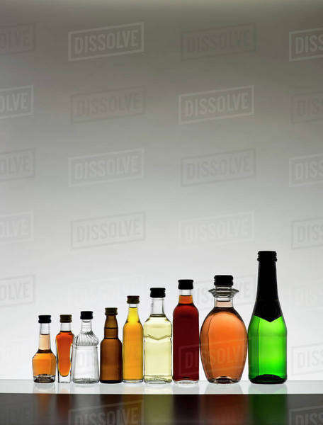 A line of various miniature bottles of alcohol without labels, back lit ...