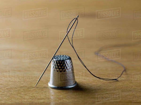 A threaded needle balanced against a shiny metal thimble - Stock Photo ...