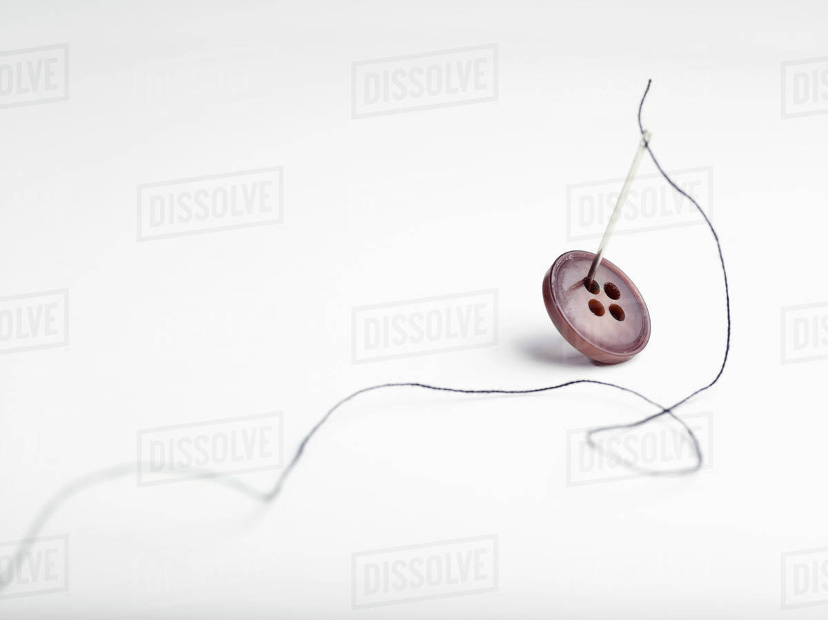 A threaded needle and button - Stock Photo - Dissolve