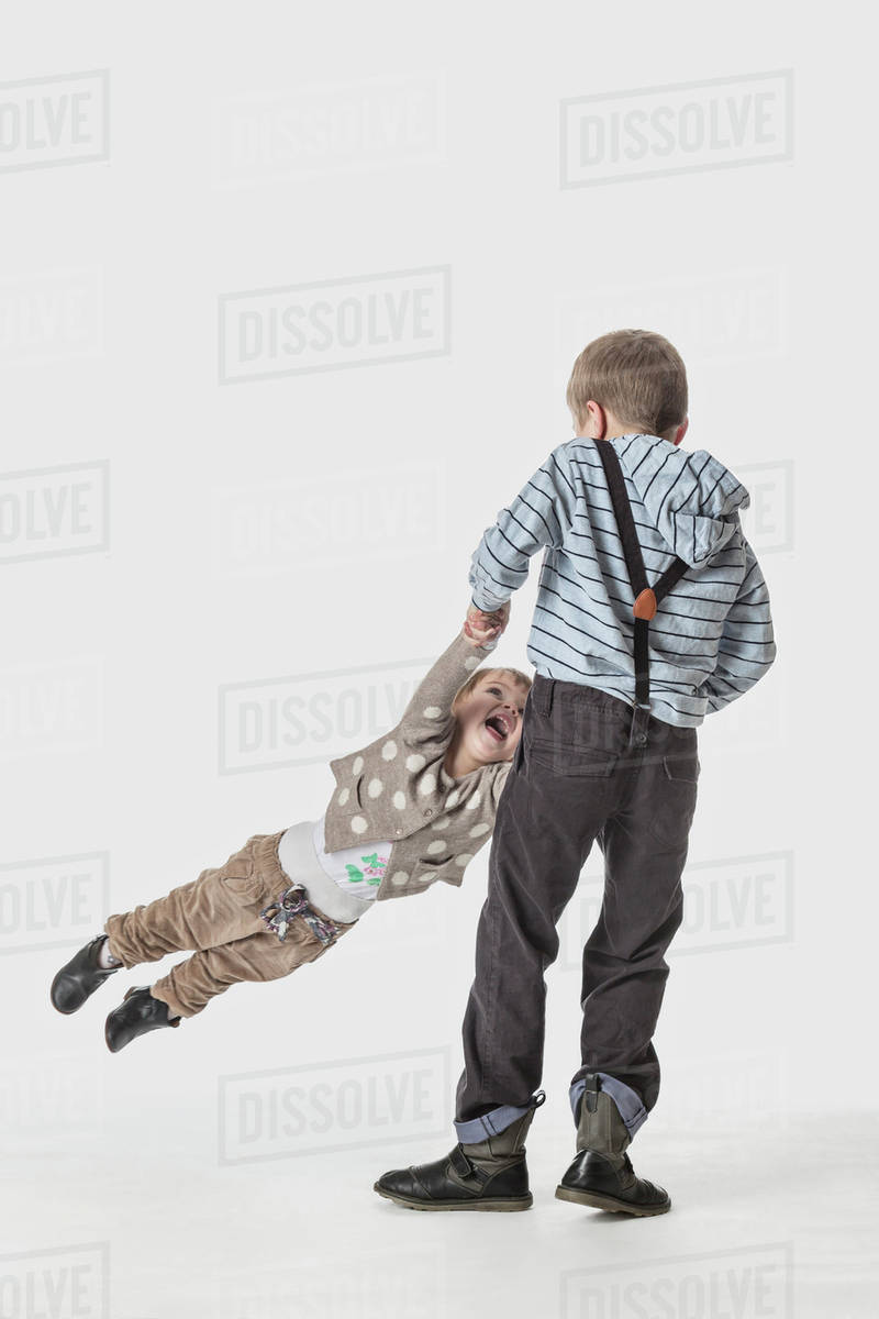 Rear view of brother spinning sister against white background - Stock ...