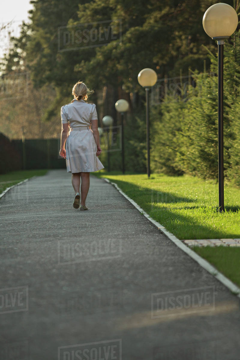 Full length rear view of woman walking on footpath - Stock Photo - Dissolve
