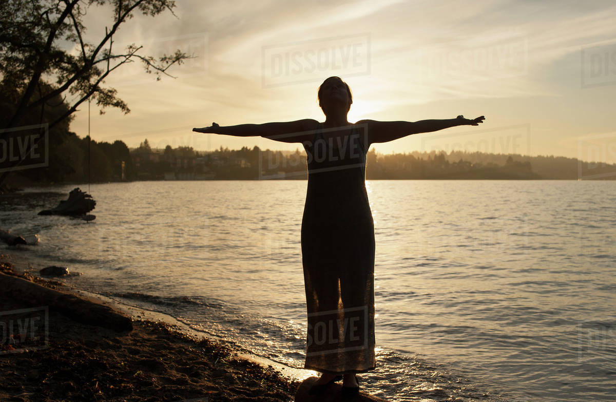 Full length of young woman standing with arms outstretched on lakeshore ...