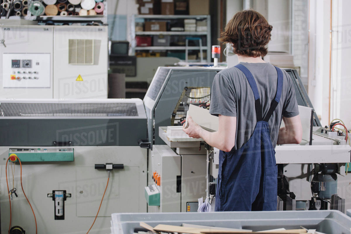 Rear view of young male worker operating machine in factory - Royalty ...