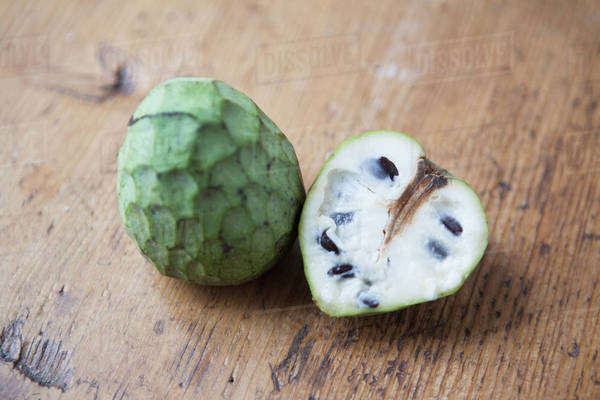 High angle view of whole and halved cherimoya on wooden table - Royalty ...