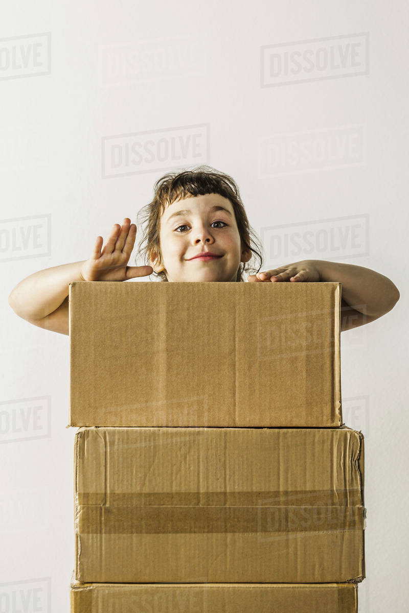 Portrait of happy girl tapping while standing behind stacked boxes ...