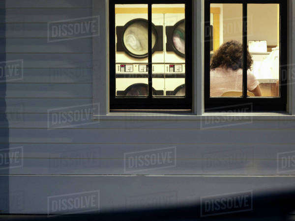A woman in a laundry mat, rear view through window - Stock Photo - Dissolve