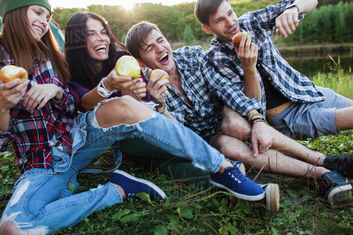 Happy friends falling on each other while having apple in forest ...