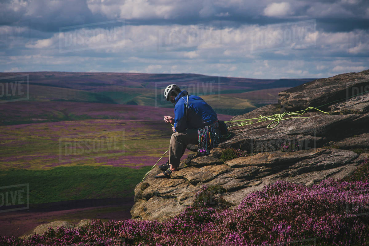 Side view of rock climber sitting on cliff against cloudy sky - Stock ...