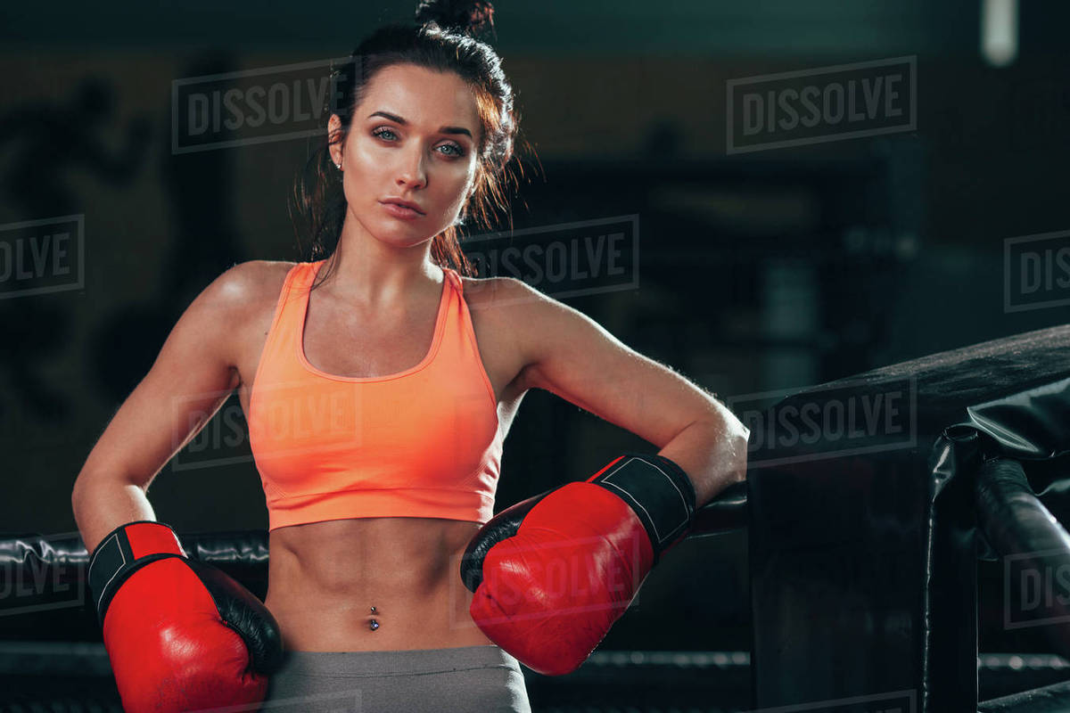 Portrait of confident female boxer leaning on rope in boxing ring ...