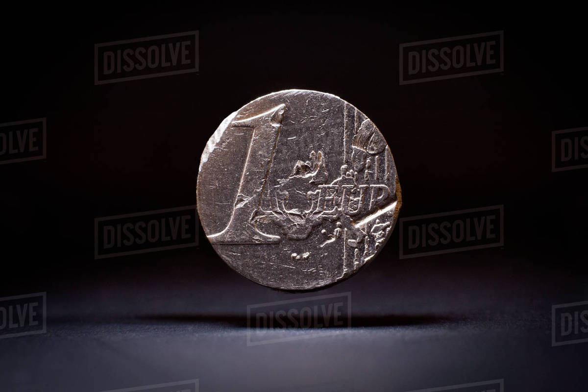 Close-up of damaged one euro coin levitating against black background ...