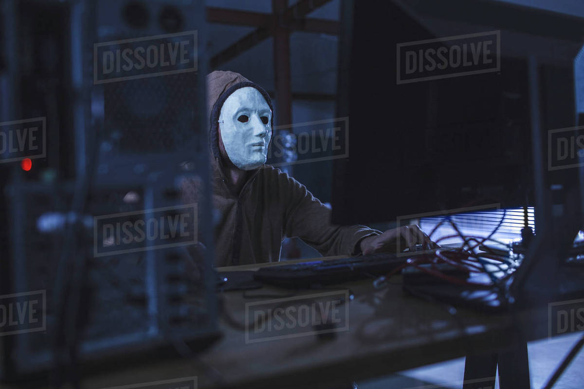 Man wearing mask and hood using computer at table - Royalty-free Stock ...