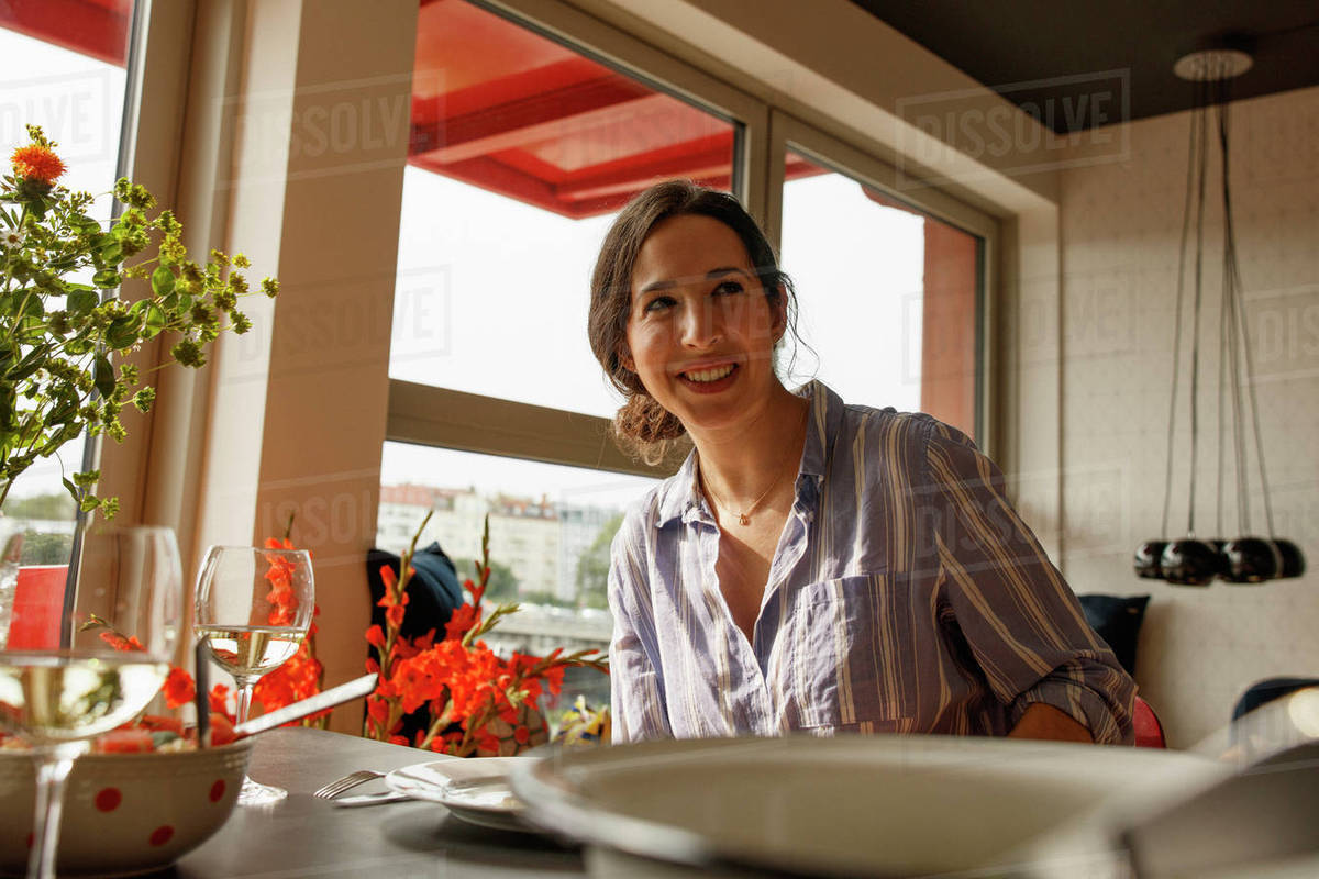 Happy young woman looking away while sitting at dining table - Stock ...