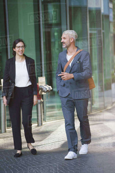 Happy business people talking while walking on sidewalk in city ...