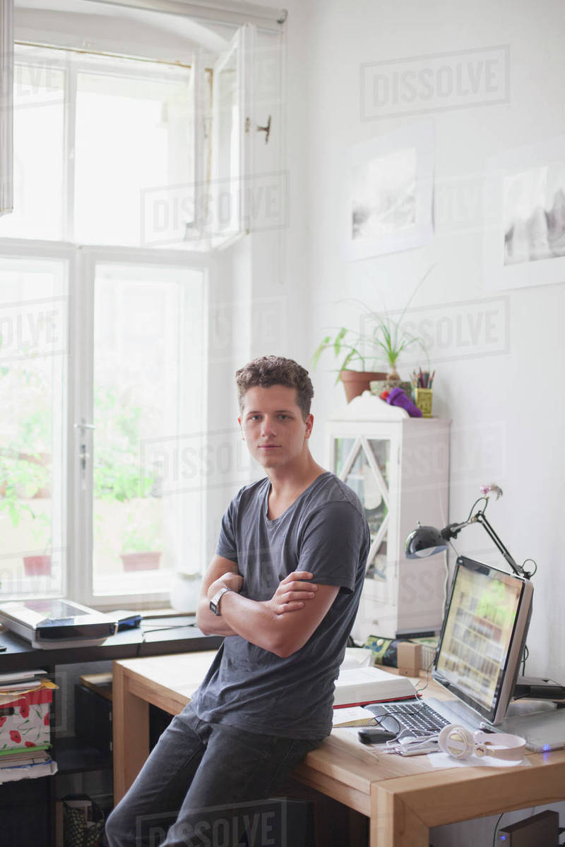 Portrait of handsome man leaning with arms crossed on table at home ...