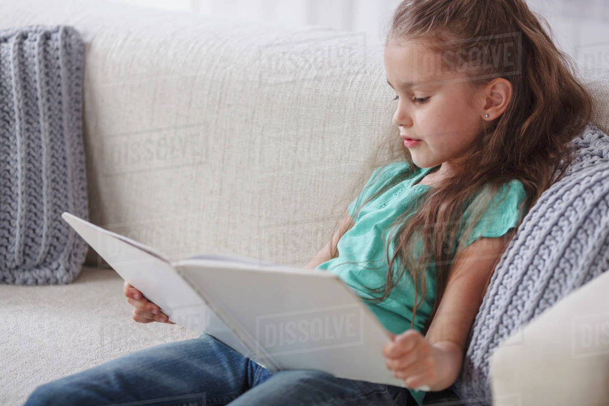 Girl reading book while sitting on sofa at home - Royalty-free Stock ...
