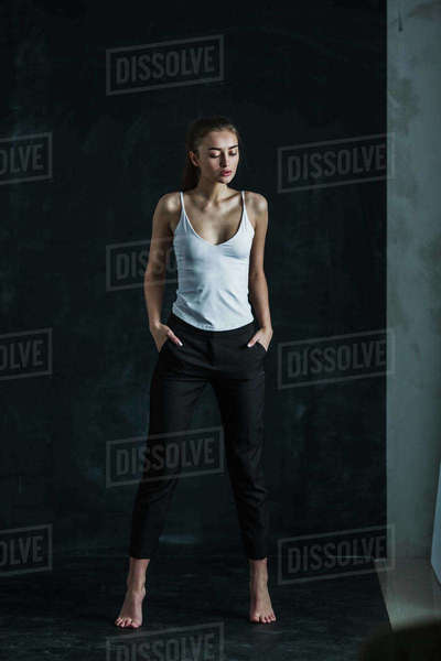 Full length of young fashion model standing against black backdrop ...
