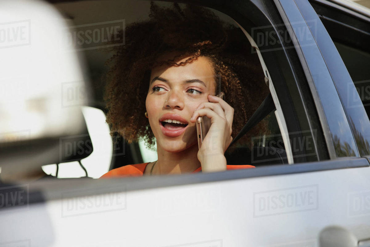 Young woman talking on smart phone and driving car - Stock Photo - Dissolve