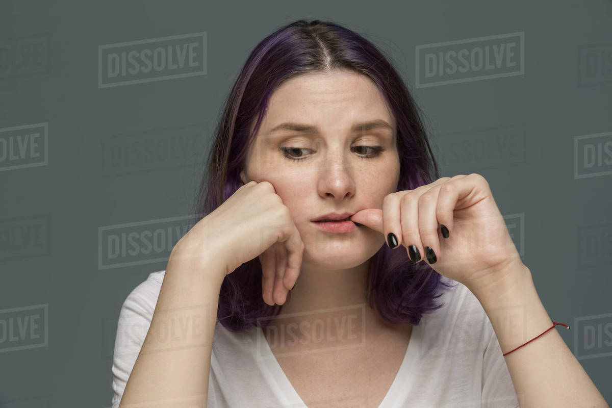 Portrait of a young woman with dyed hair biting thumb and looking down ...