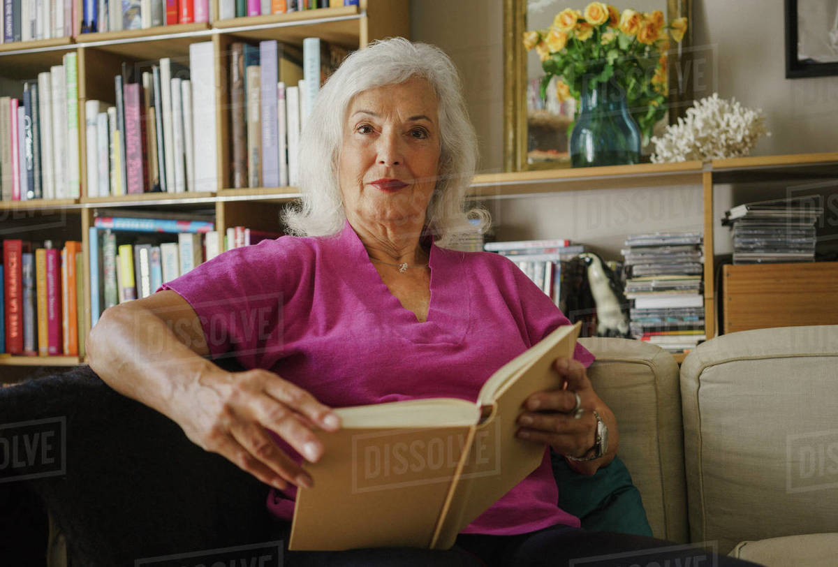 Portrait confident senior woman reading book in living room - Royalty ...