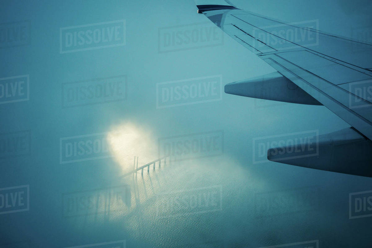 Airplane wing flying through clouds over water - Stock Photo - Dissolve