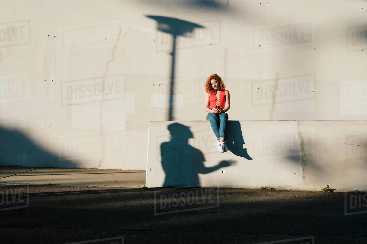 Shadow looking up at young woman using smart phone on urban wall ...