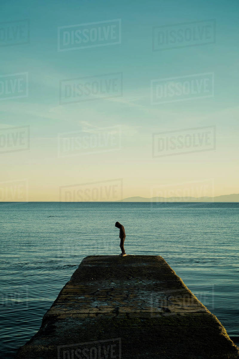 Boy in hoody standing on ocean pier, Victoria, British Columbia, Canada ...