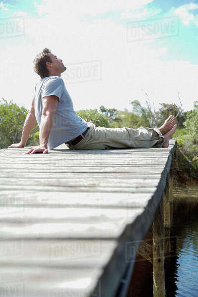 Portrait of barefoot man sitting on a boardwalk by a river - Stock ...