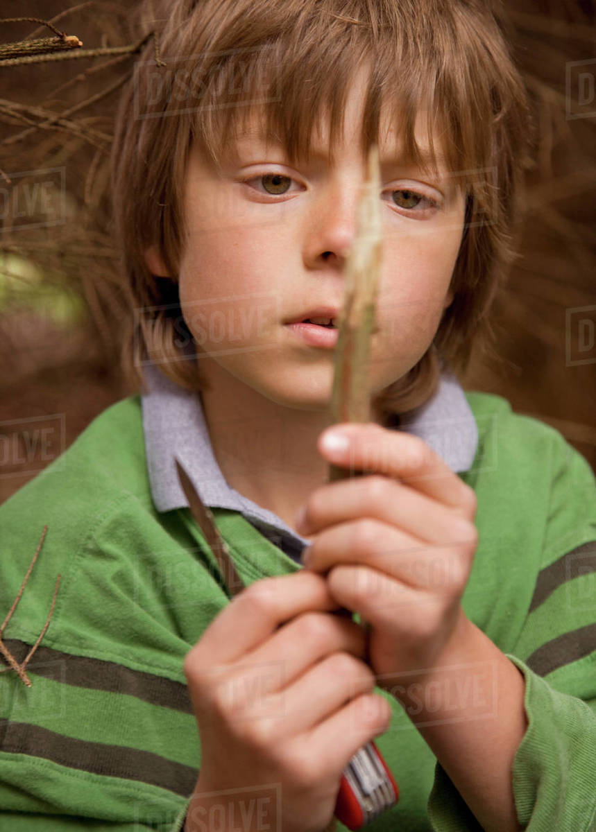 Close up of young boy sharpening a wooden stick in a campsite - Royalty ...
