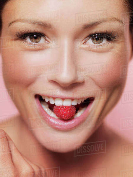 A woman holding a raspberry between her teeth, close-up - Stock Photo ...