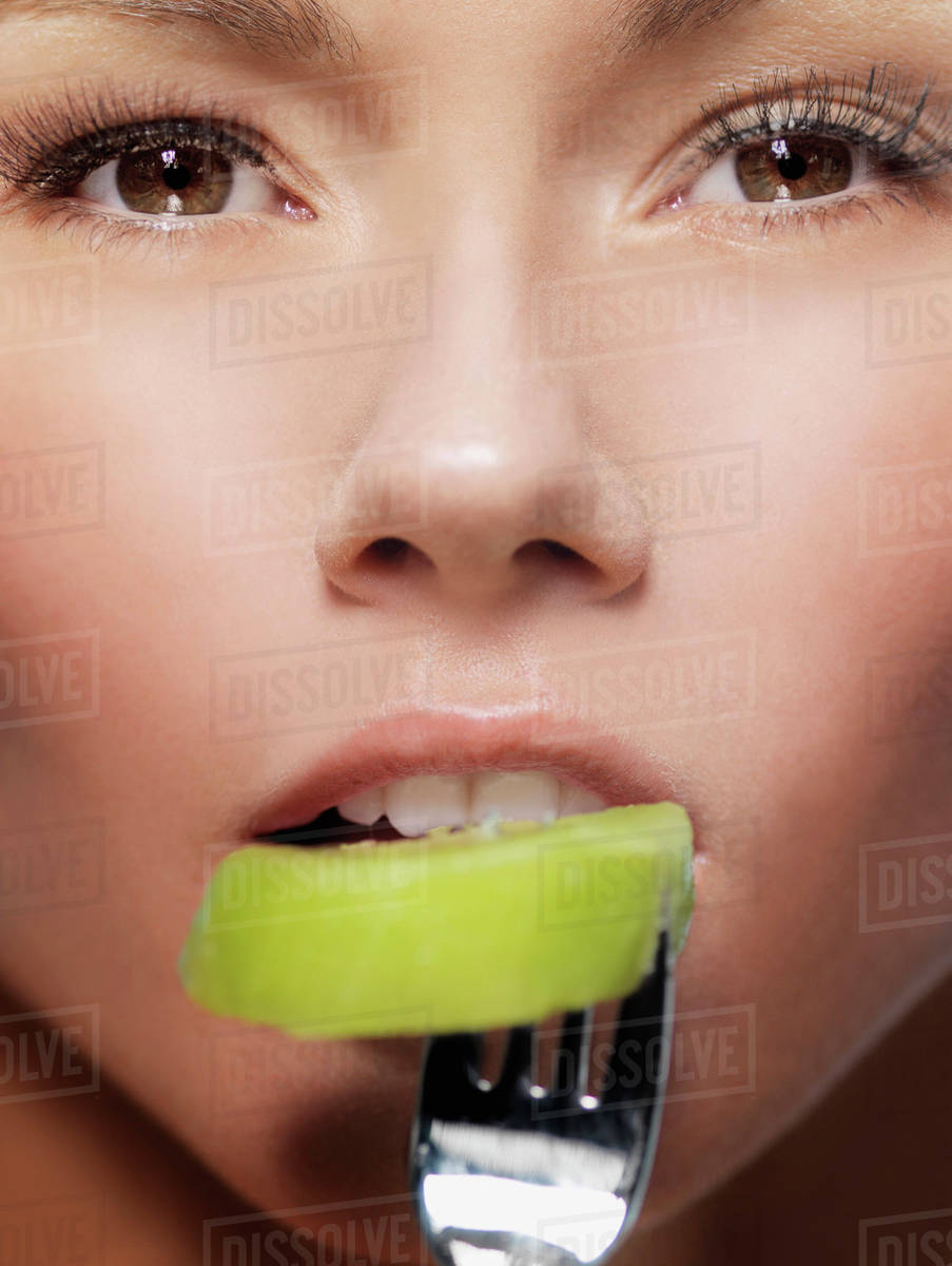 A woman biting a slice of kiwi on a fork, close-up of face - Stock ...